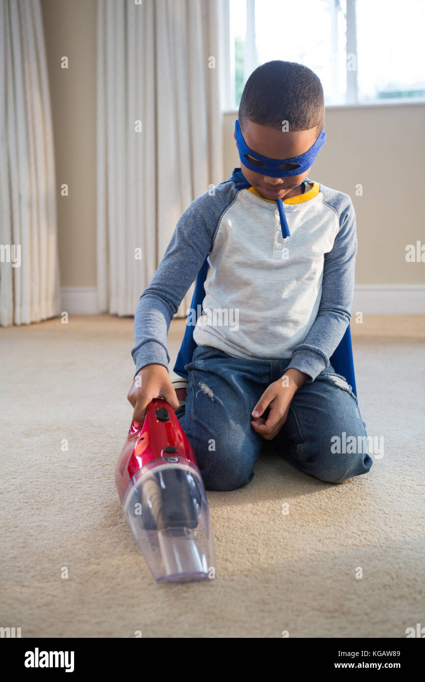 Boy in superhero costume cleaning a floor with vacuum cleaner at home ...