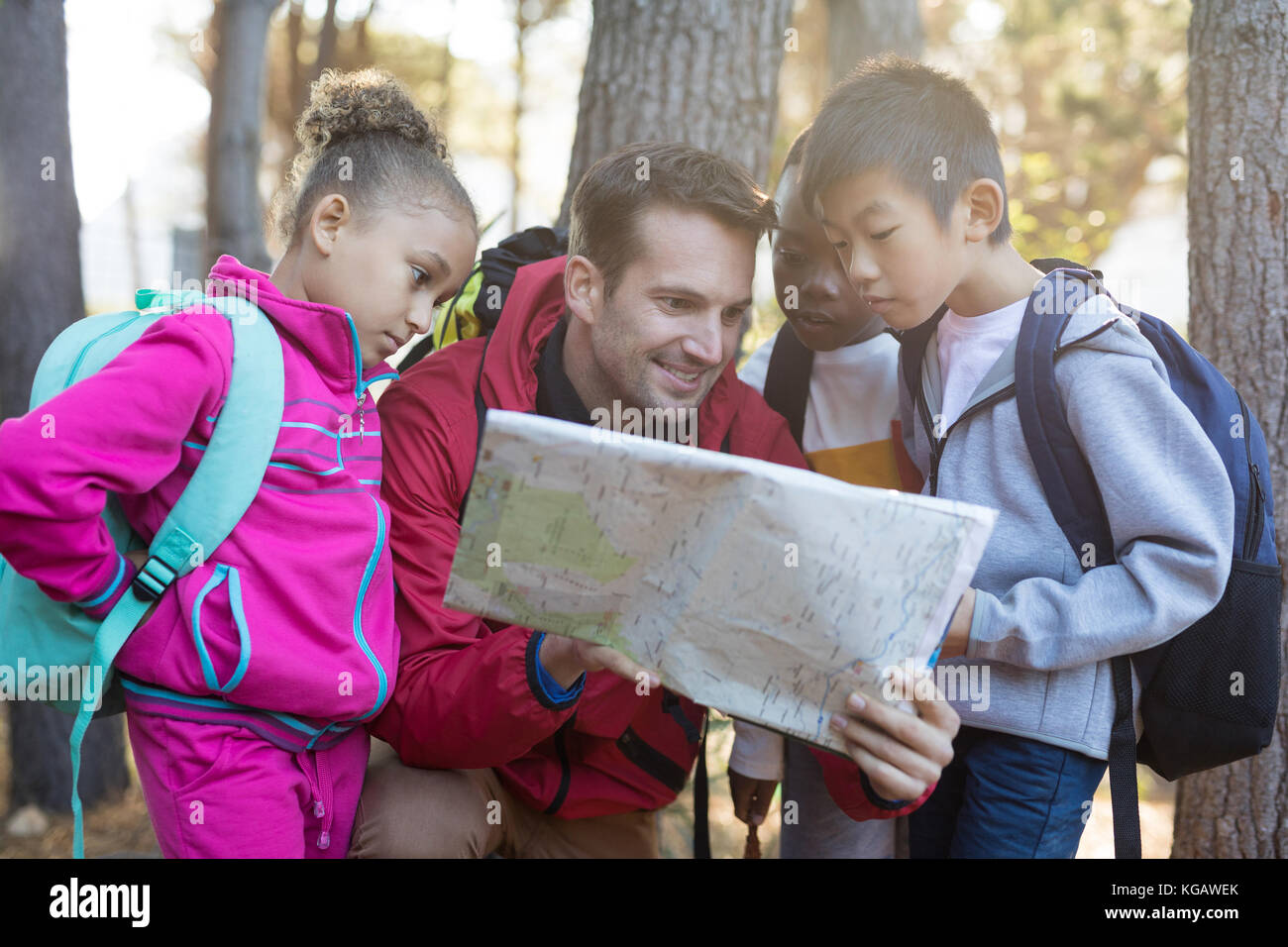 Teacher and kids reading map in forest Stock Photo - Alamy