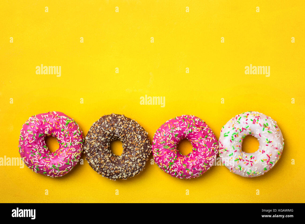 Four donuts in line on yellow background. Top view with copy space ...