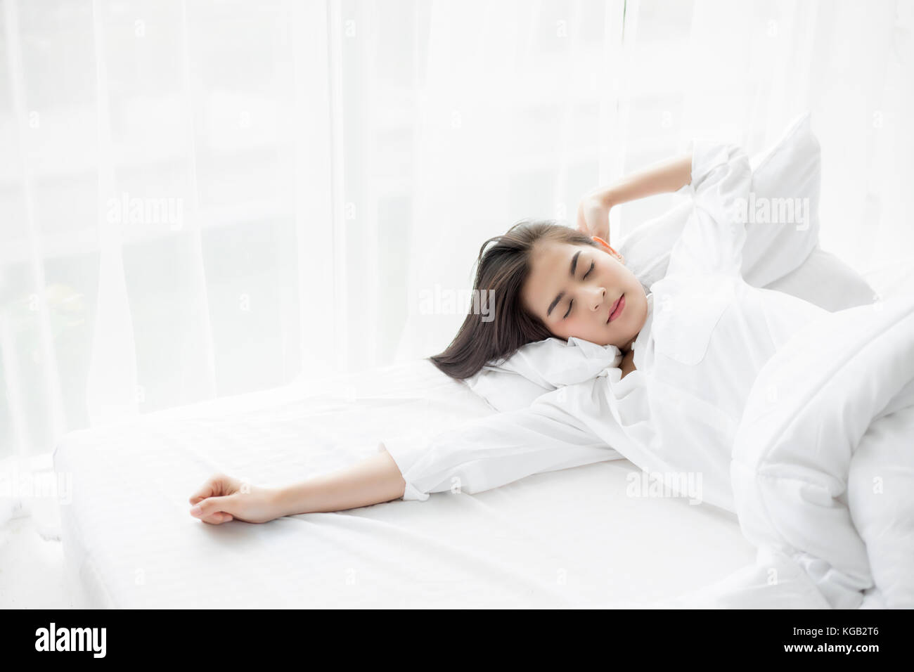 Asian woman Beautiful young smiling woman sitting on bed and stretching ...