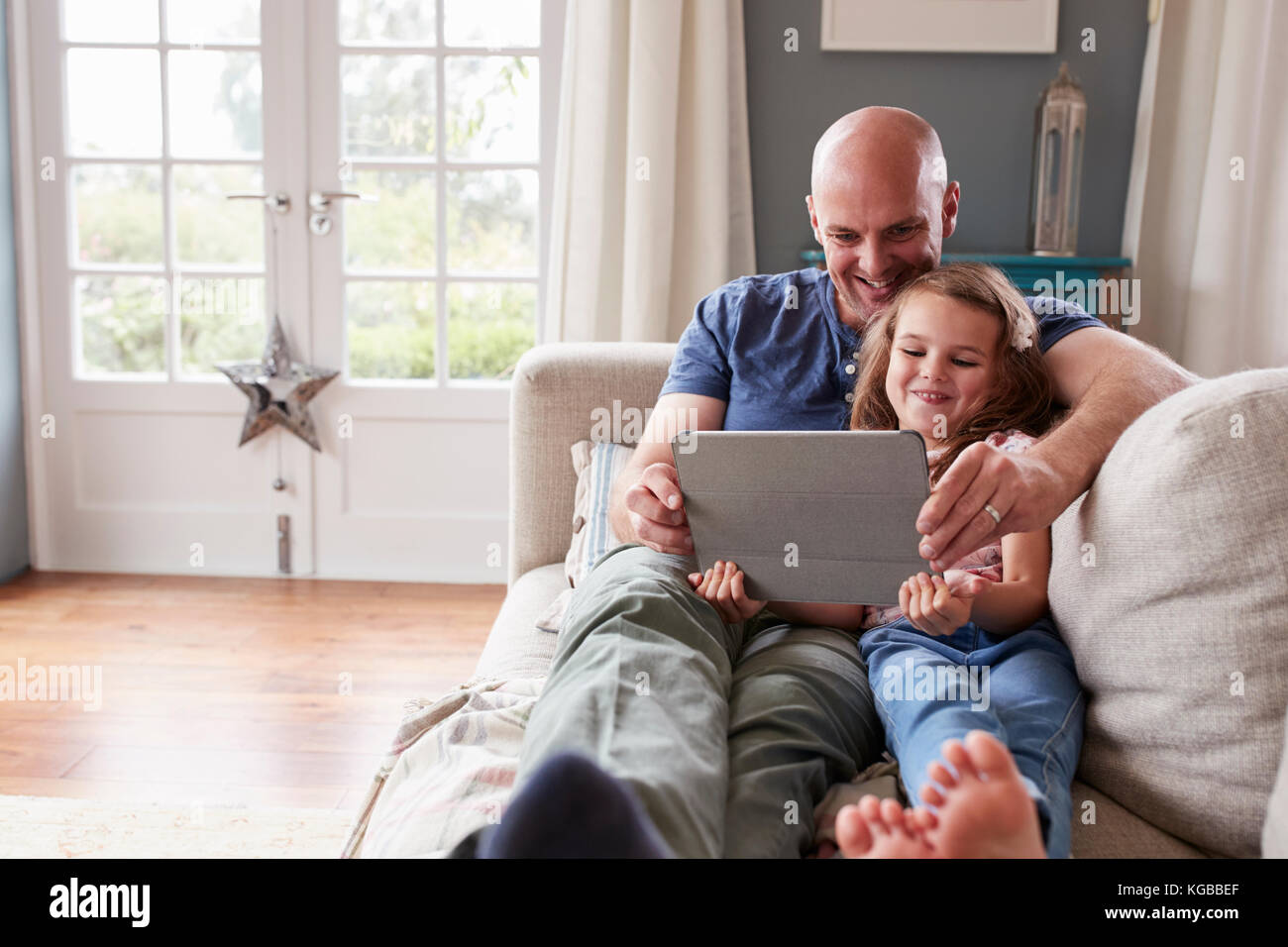 Dad and daughter on couch using a tablet computer, closer in Stock ...