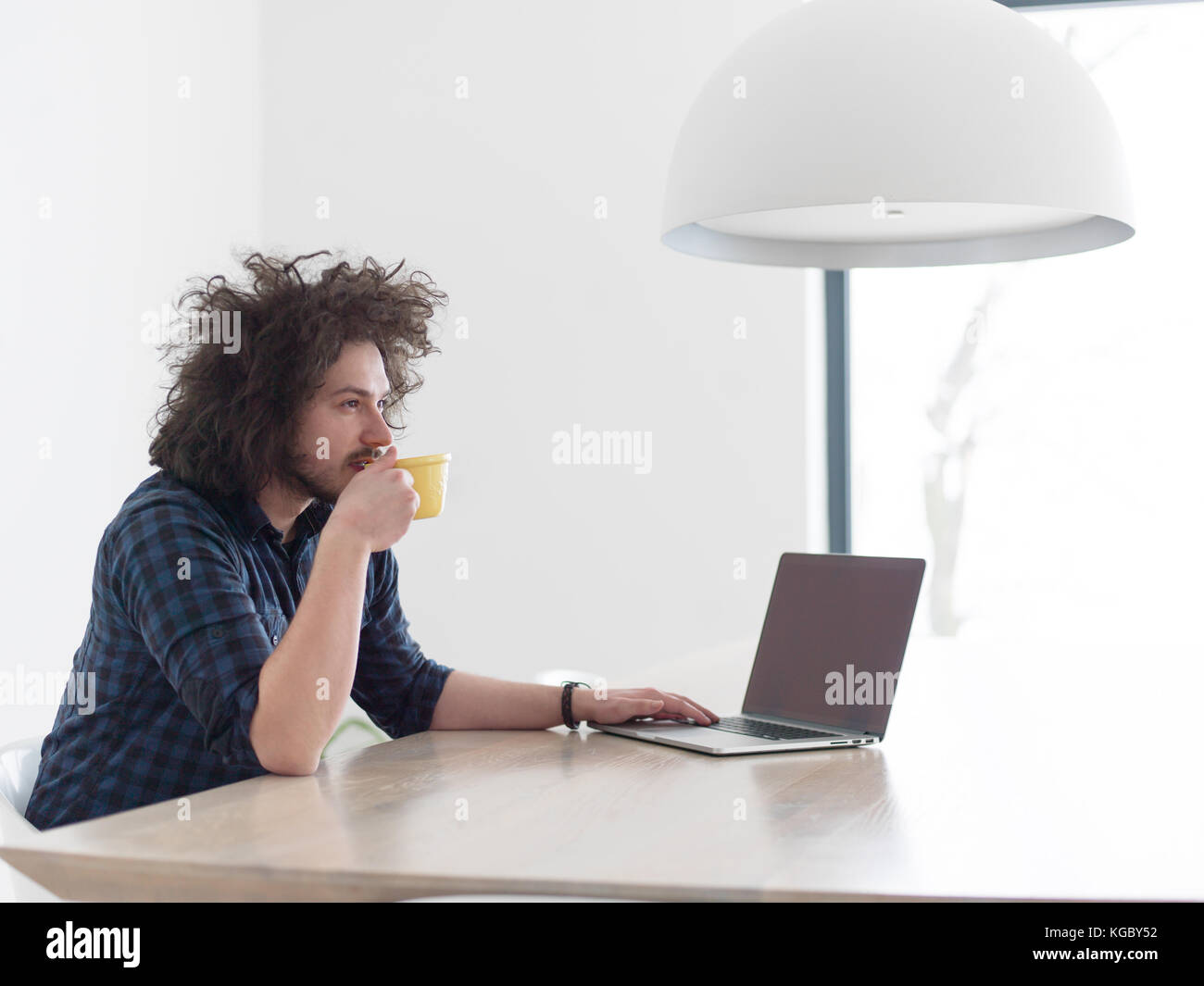 young man drinking coffee while working from home on his laptop ...