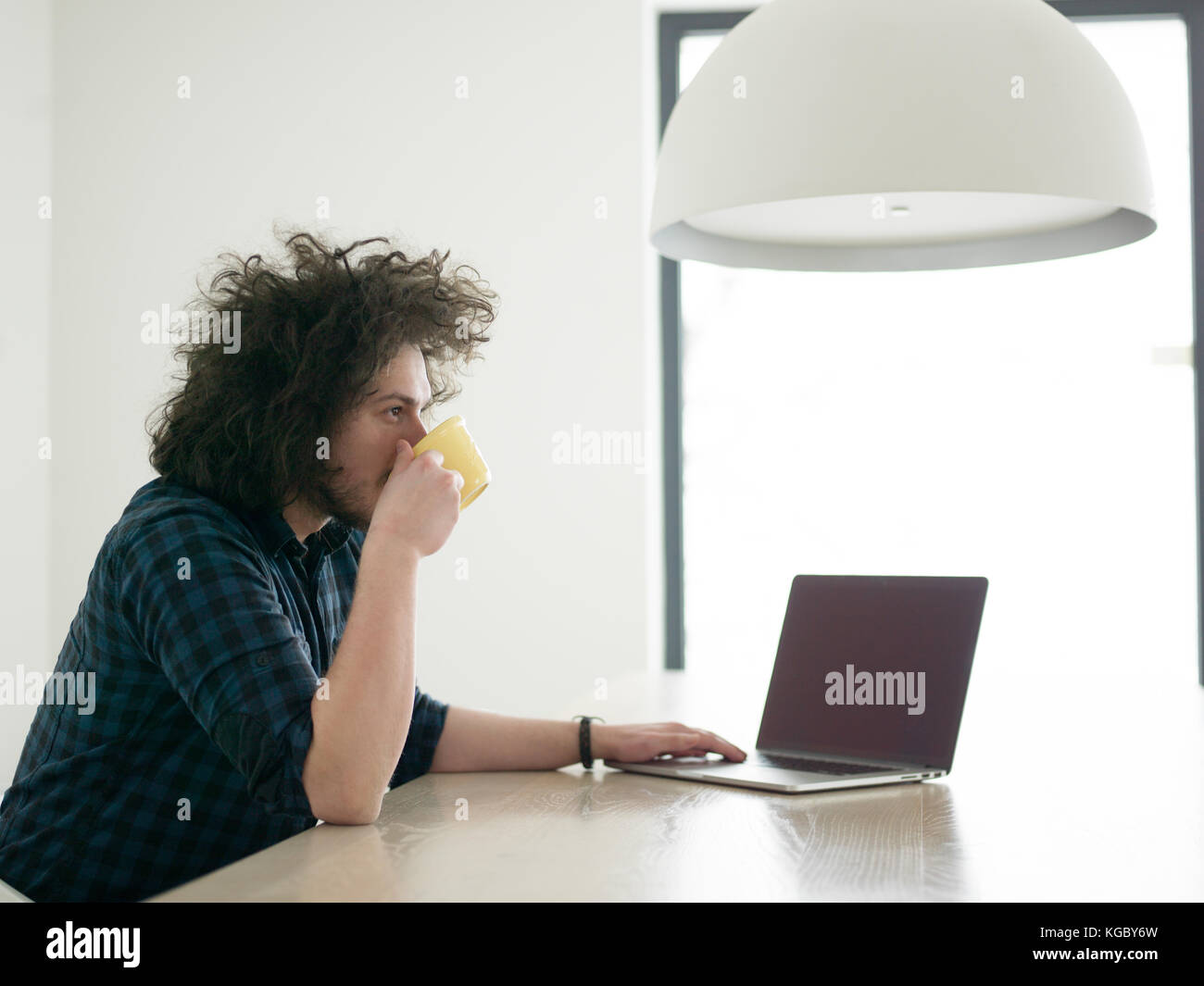 young man drinking coffee while working from home on his laptop ...