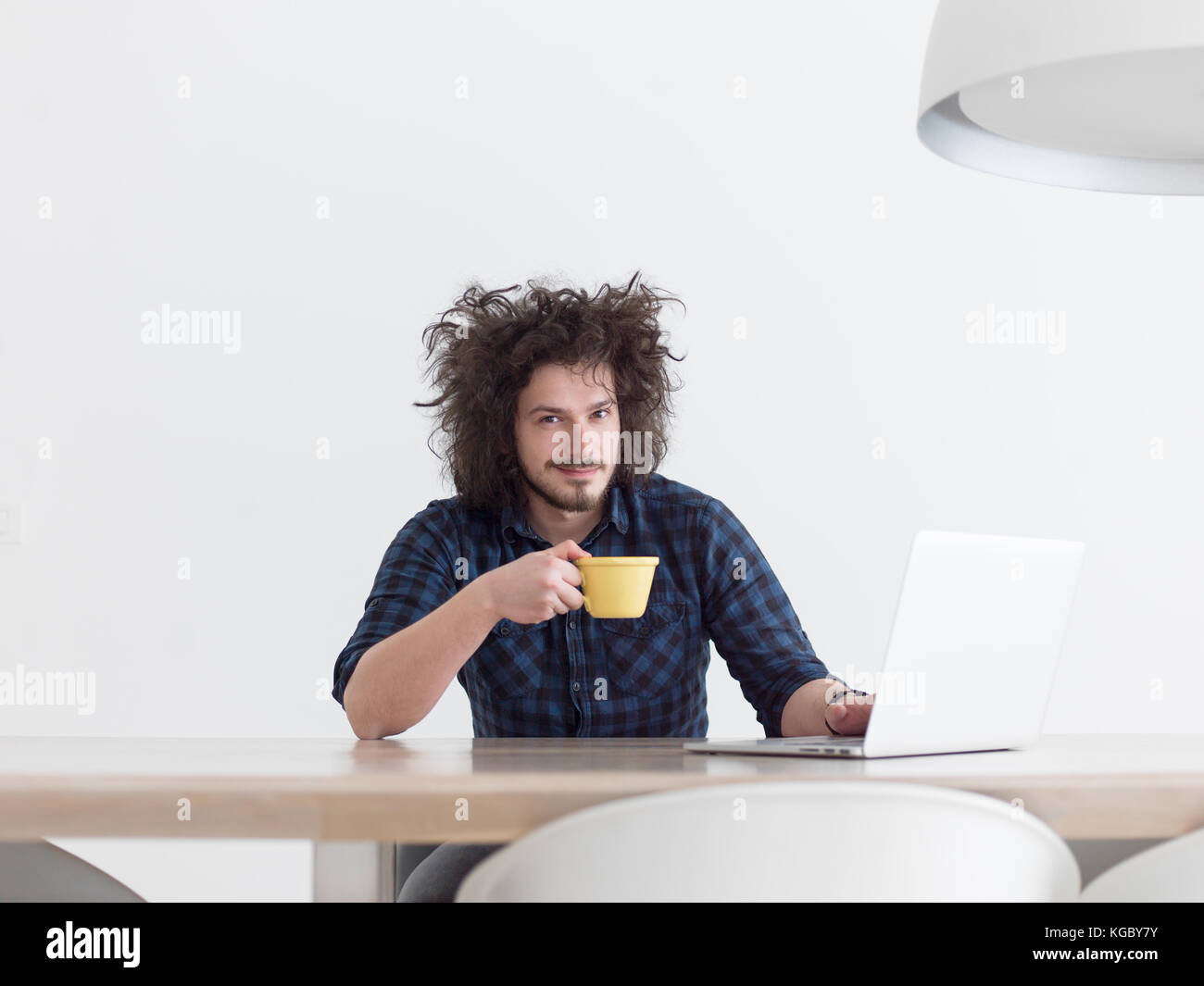 young man drinking coffee while working from home on his laptop ...