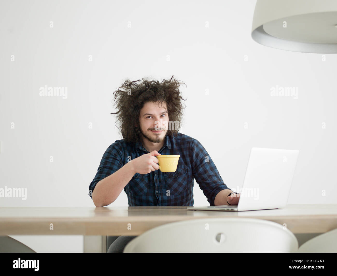 young man drinking coffee while working from home on his laptop ...
