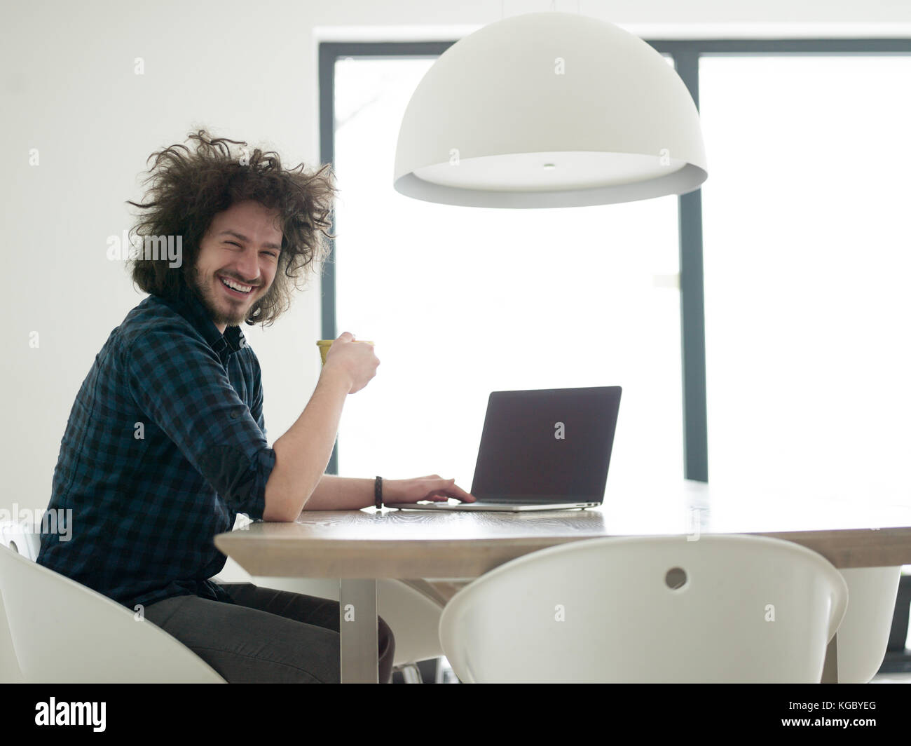 young man drinking coffee while working from home on his laptop ...