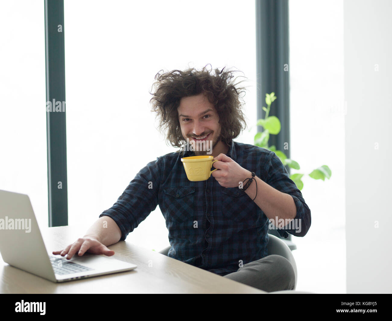 young man drinking coffee while working from home on his laptop ...