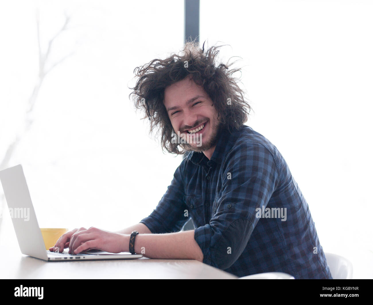 young man drinking coffee while working from home on his laptop ...