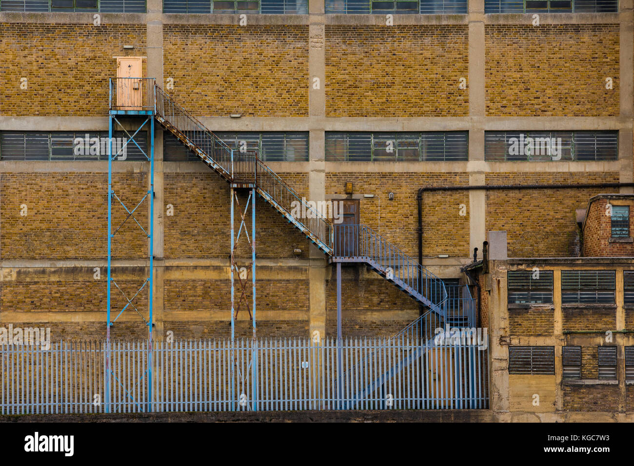 Run down industrial building yellow brick facade with blue rusty fire ...