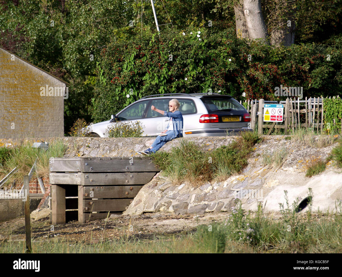 Elderly lady artist sat on wooden jetty at Bosham Harbour, Hampshire ...