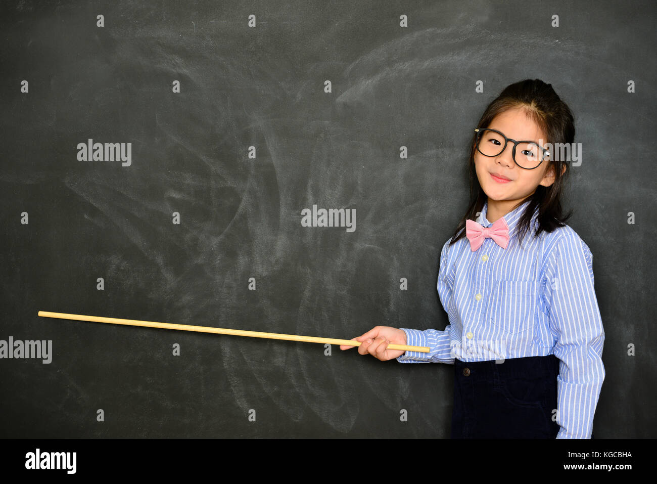 smiling pretty little teacher using stick pointing chalkboard empty ...