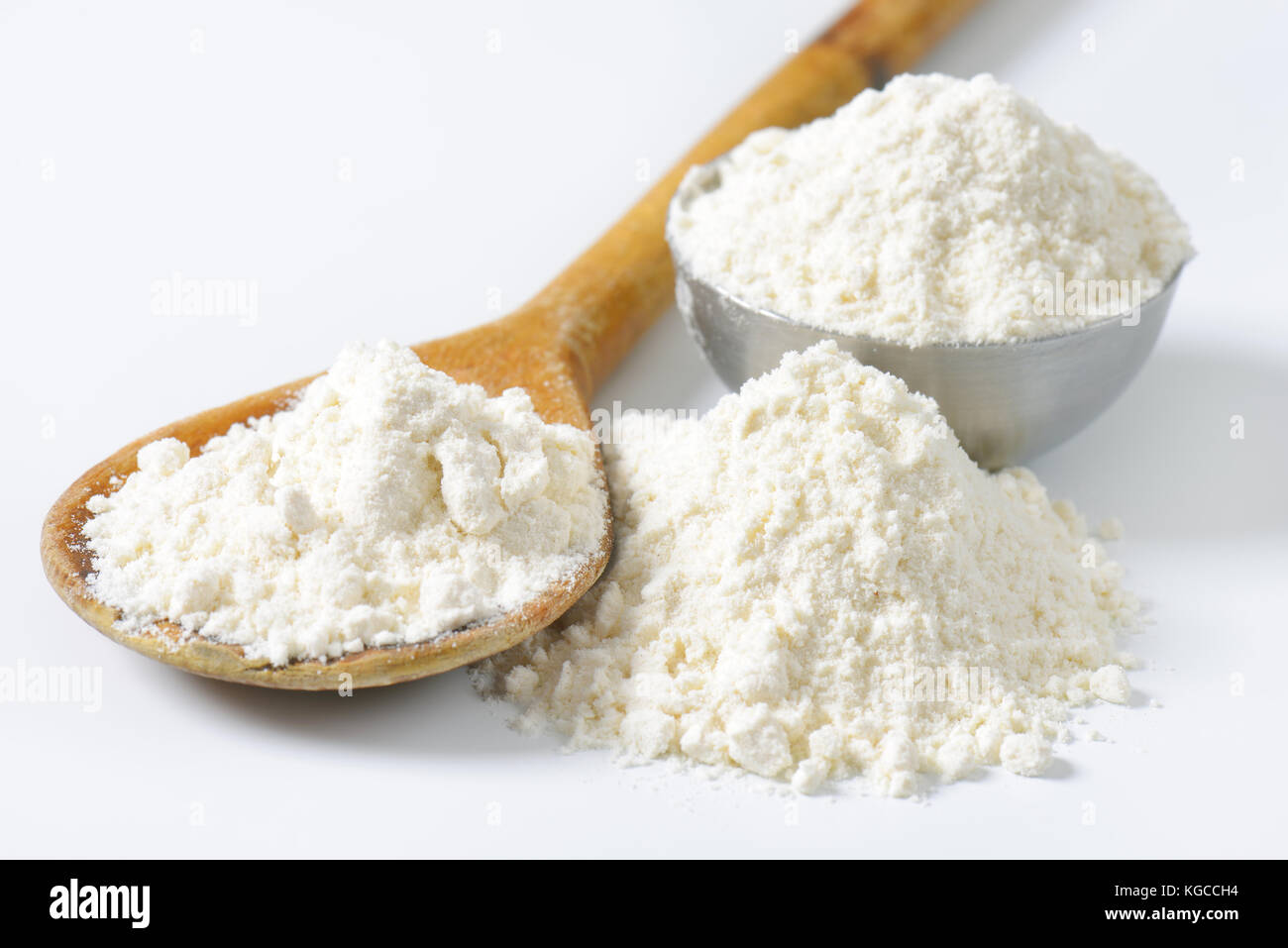 close up of soft wheat flour on wooden spoon and in metal bowl on white ...