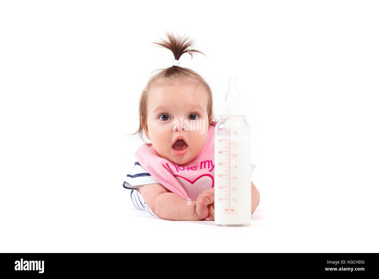 cute confused baby girl in white shirt and pink bib holds bottle Stock ...