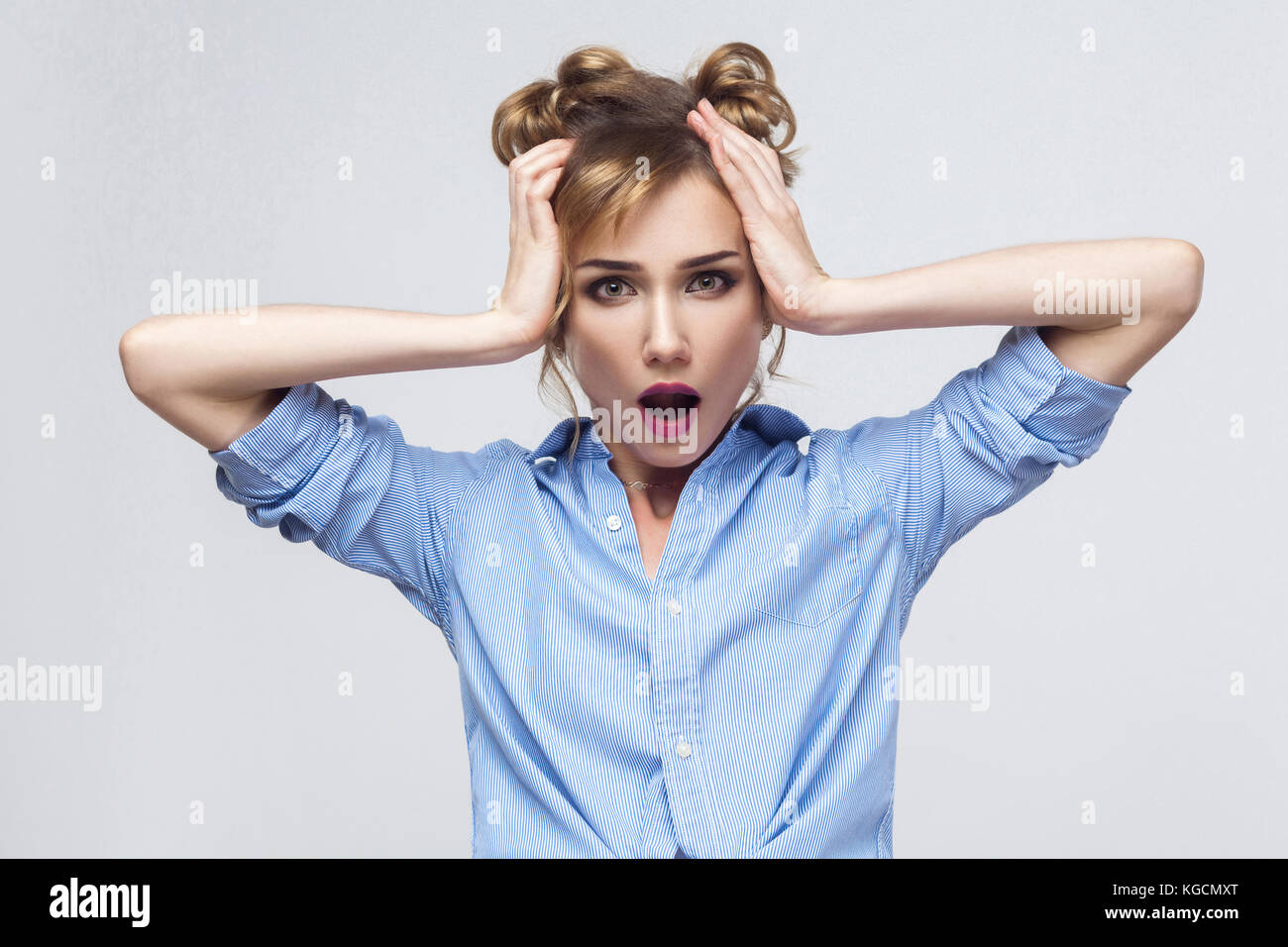 Blonde woman screaming with shock, holding hands on her head. Studio ...