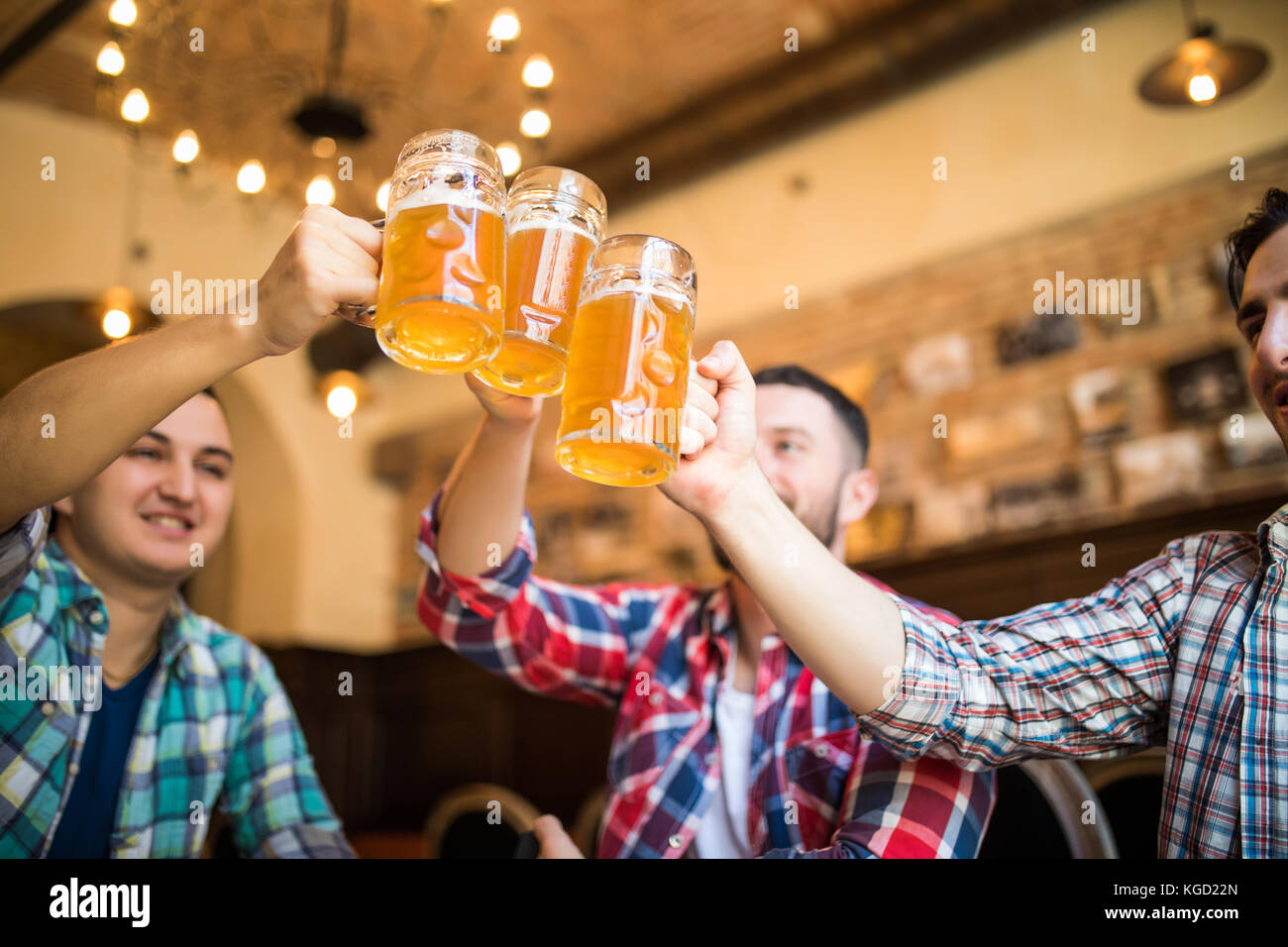 Close-up of three happy young men in casual wear toasting with beer ...