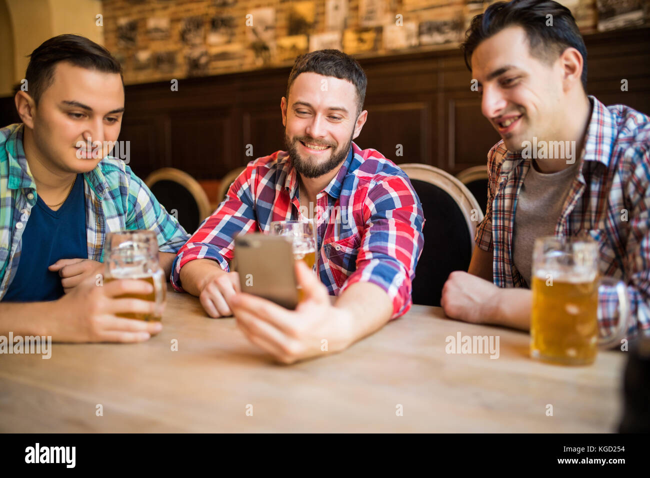 Cheerful old friends having fun with smartphone and drinking draft beer ...