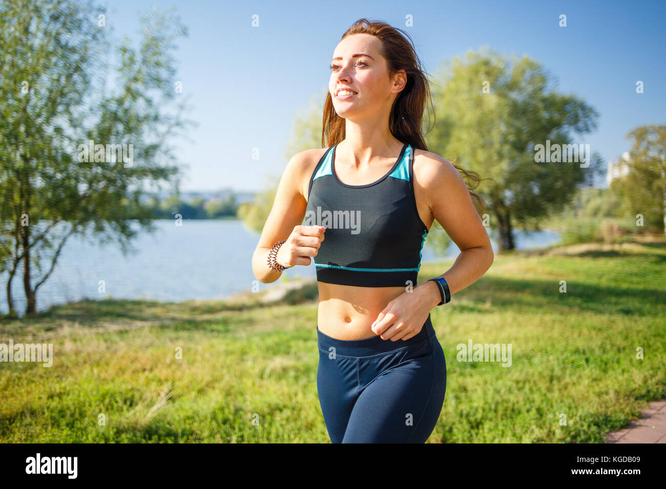 Young smiling sporty woman running in park in the morning. Fitness girl ...