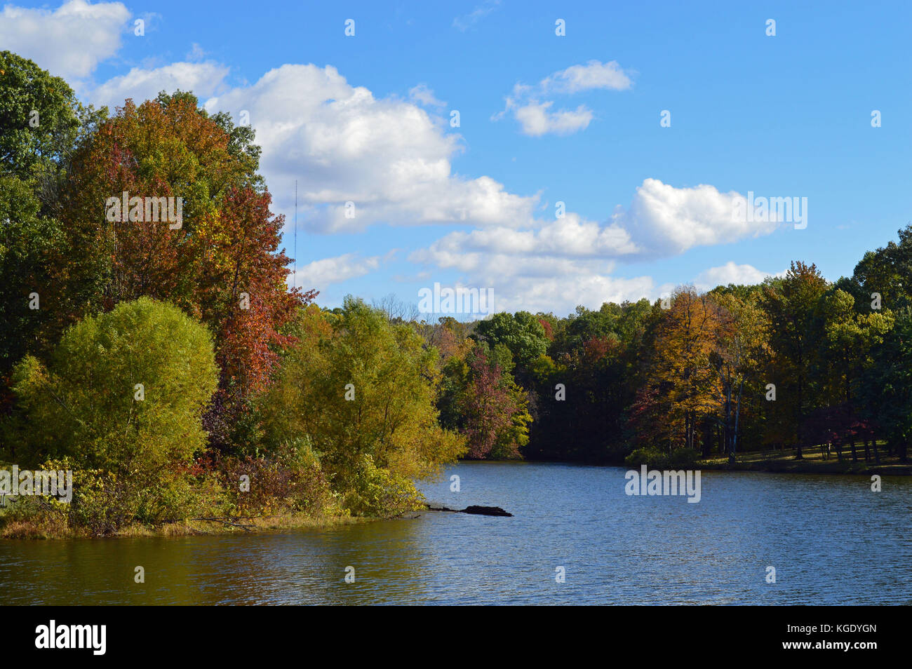 Landscape photo of a small lake lined with trees bearing autumn colors ...