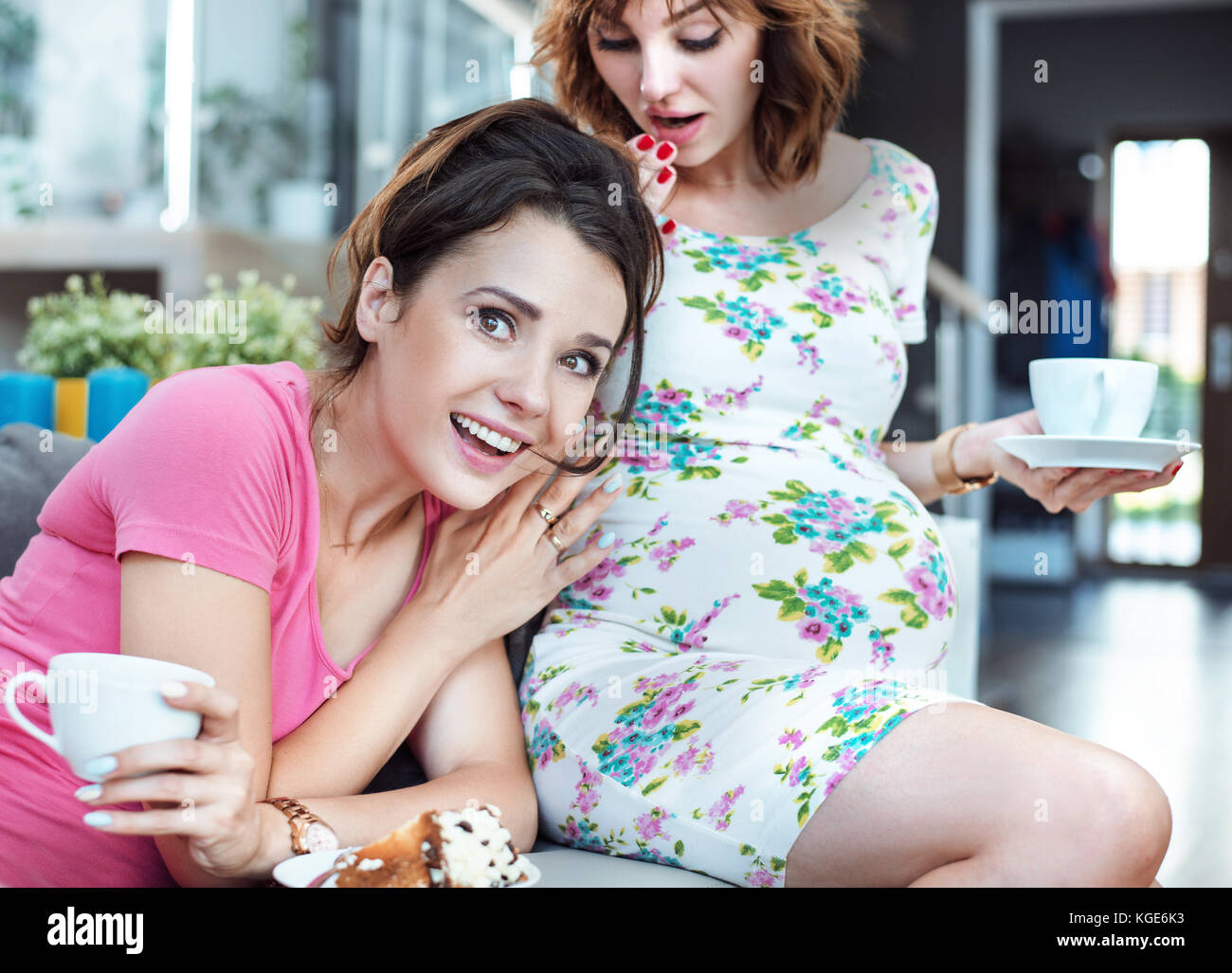 Cheerful, young girlfriend listening to the pregnant's friend belly ...
