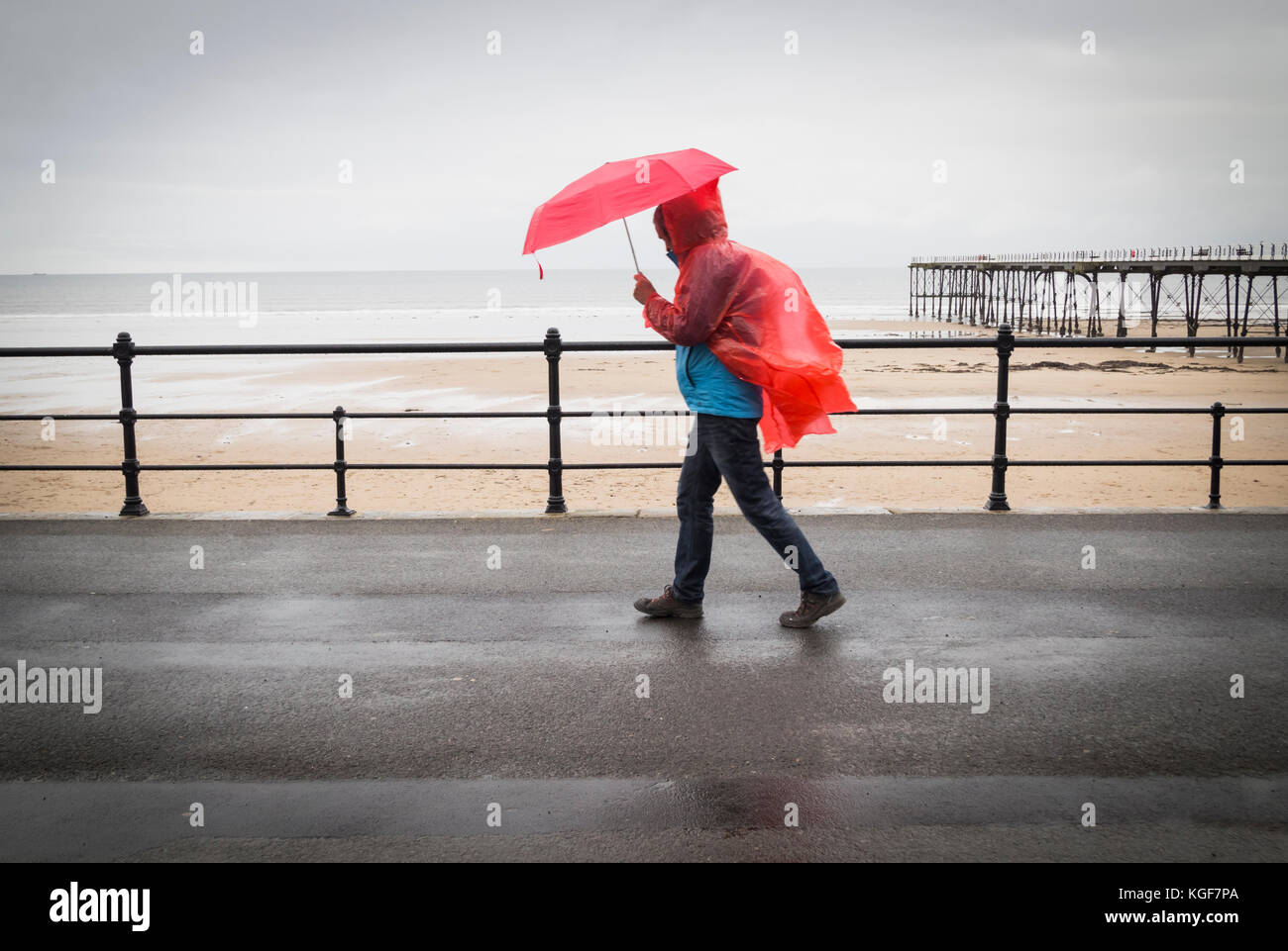 Man with red umbrella walking in the rain on beach. UK Stock Photo - Alamy