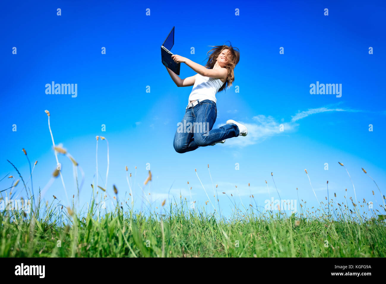 Woman holding a laptop computer jumping over blue sky Stock Photo - Alamy