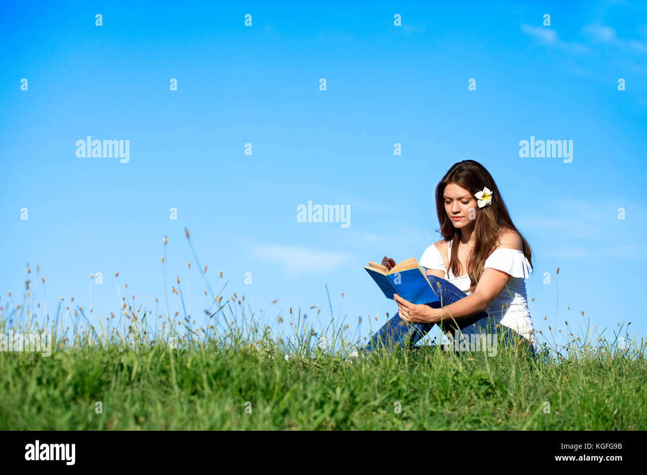 Pretty girl reading book and relaxing on grass with beautiful blue sky ...
