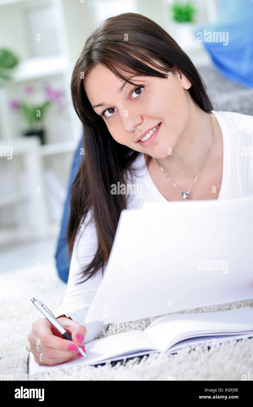 Happy teen girl learning on floor at home with books and pen in hand ...