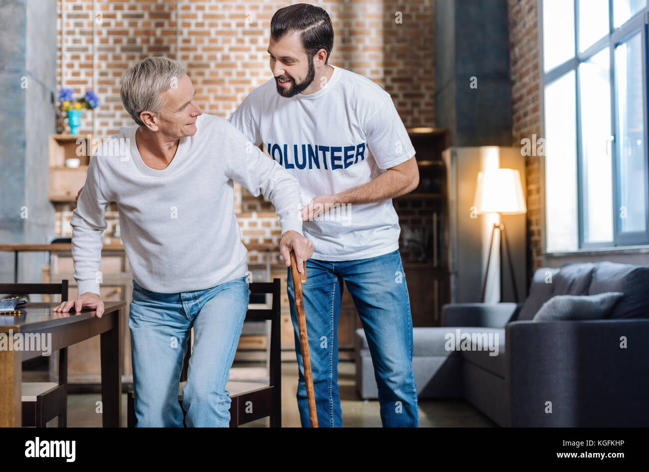 Pleasant kind volunteer supporting a senior man and helping him while ...