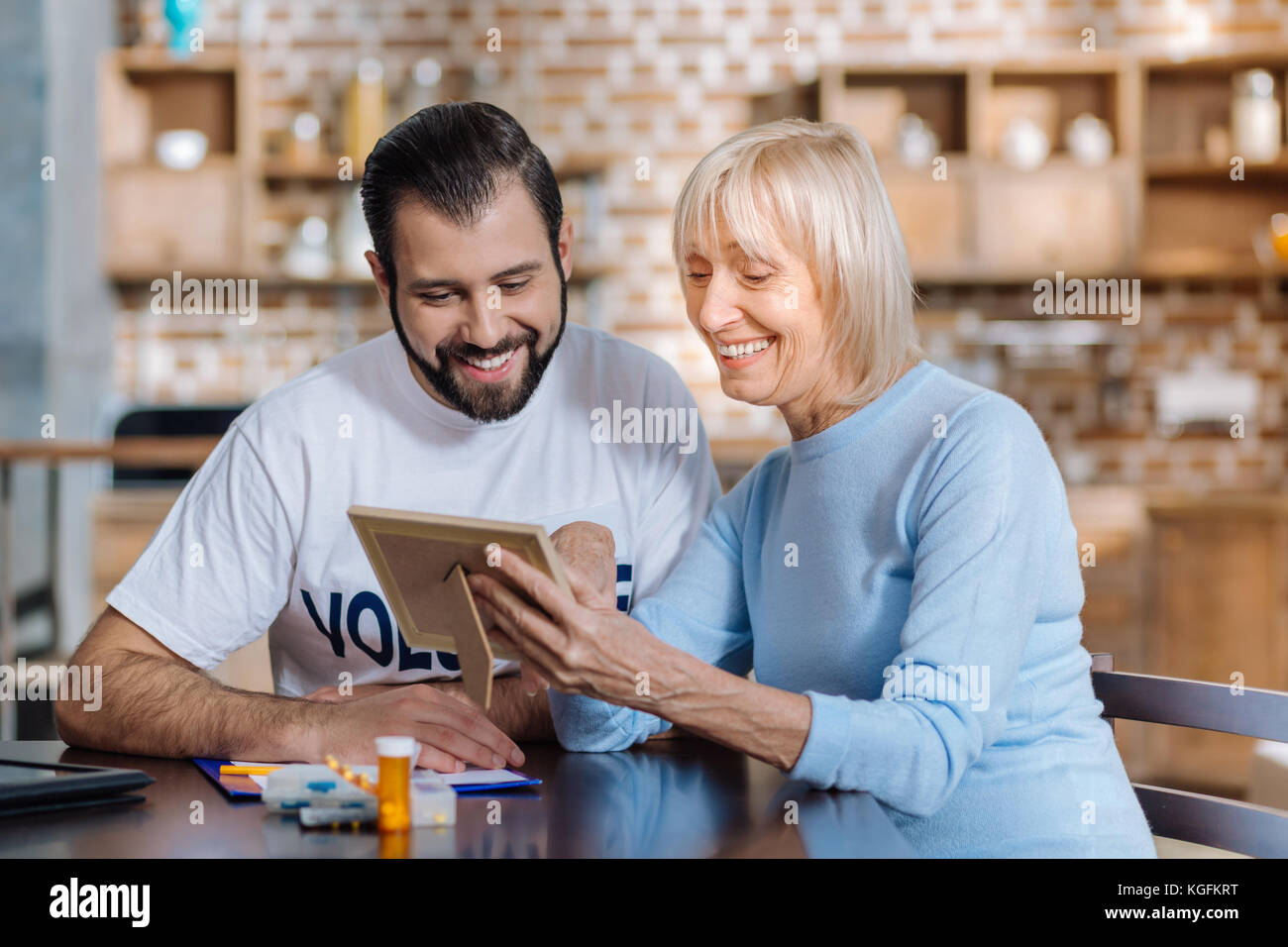 Happy volunteer looking at the old photo of a cheerful pensioner Stock ...