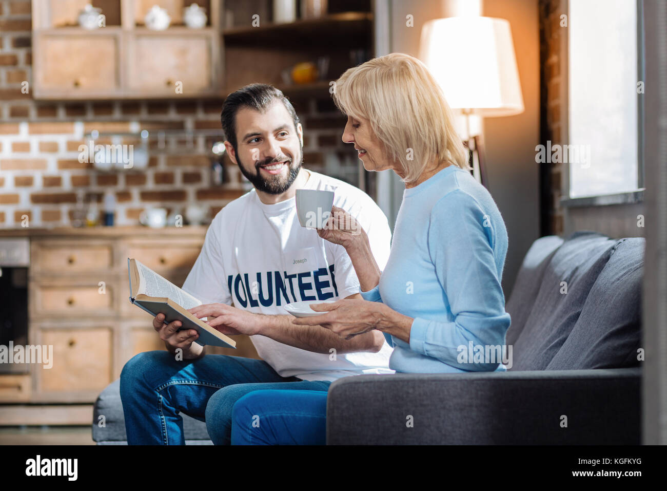 Cheerful volunteer reading a book with a senior woman Stock Photo - Alamy
