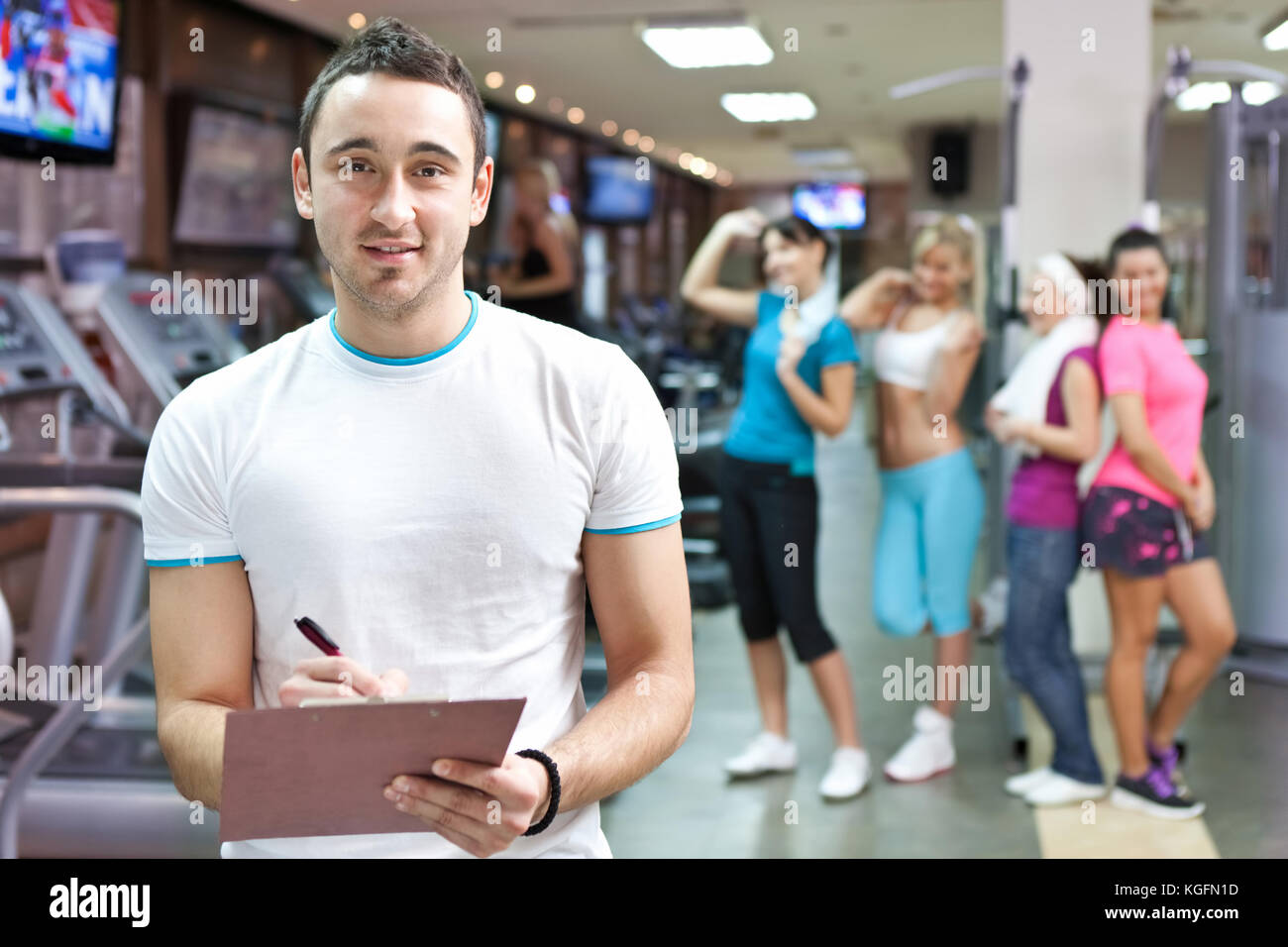 smiling young fitness instructor making note with gym girls in ...
