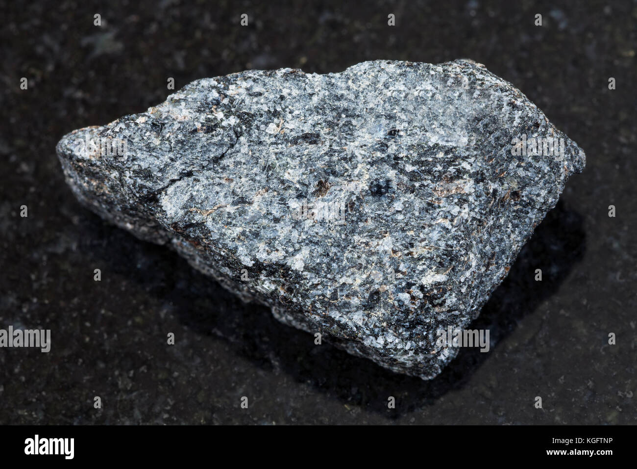 macro shooting of natural mineral rock specimen - raw nepheline syenite stone on dark granite ...