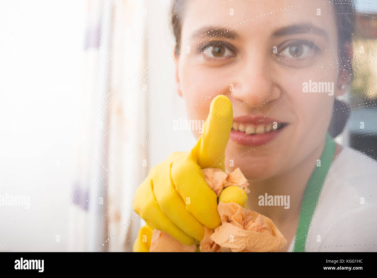 Young woman cleaning the window and pointing finger on glass in close ...