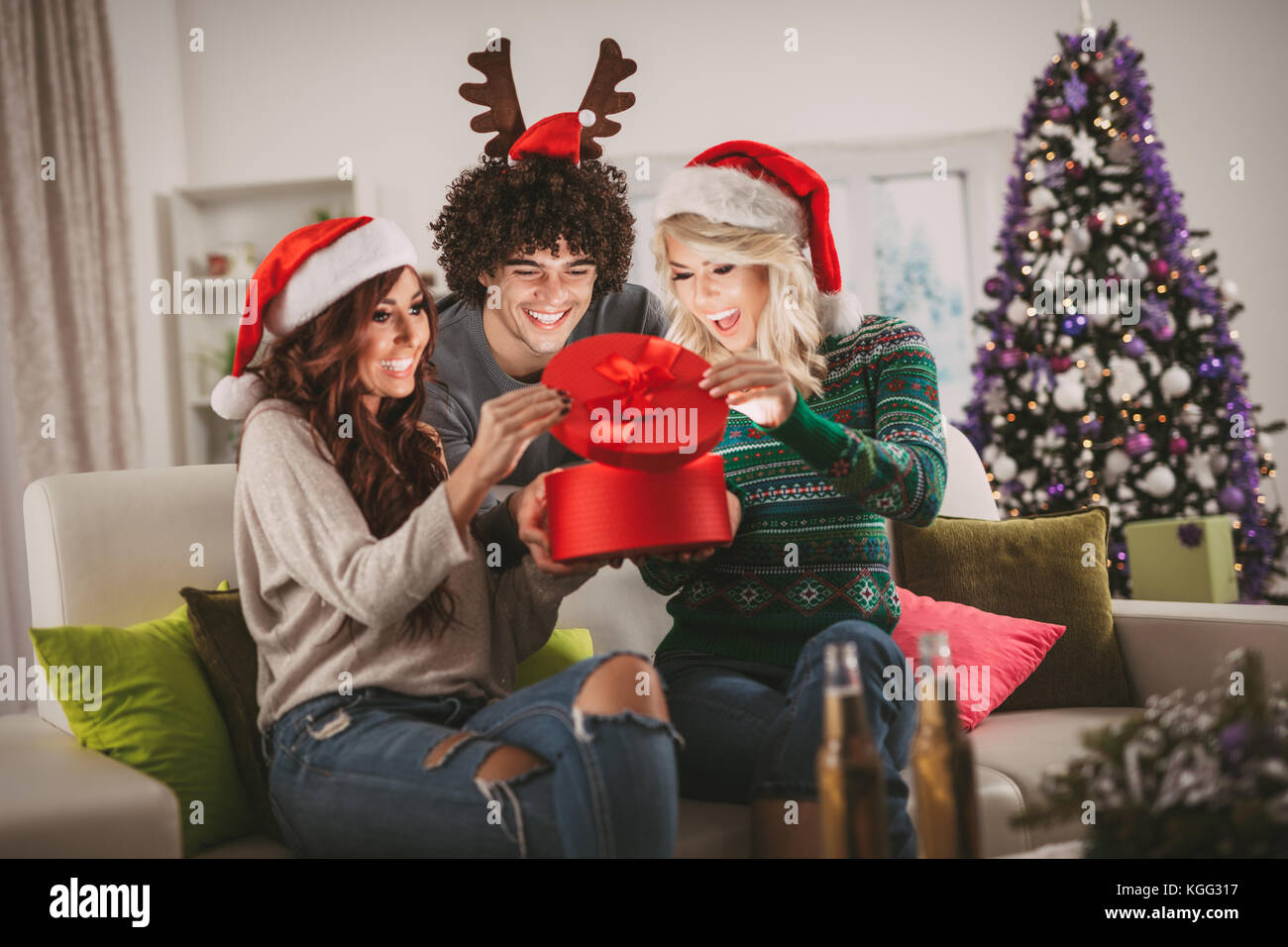 Cheerful beautiful young friends enjoying Christmas at home, opening ...
