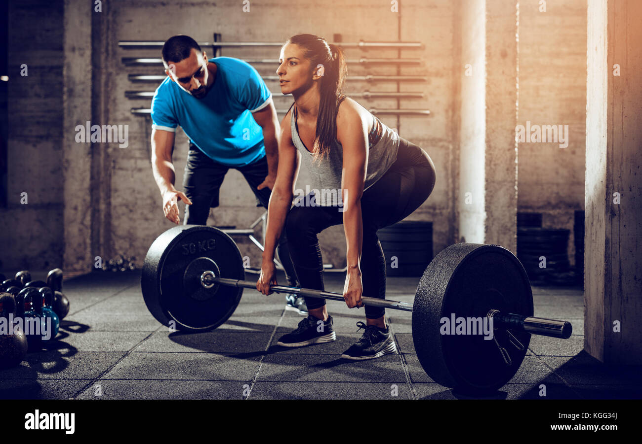 Young woman doing hard exercise at the gym with a personal trainer ...