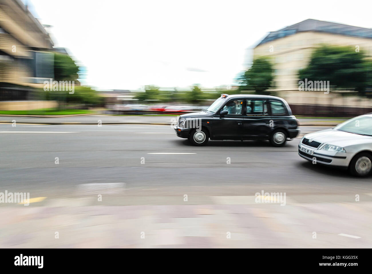 Photo of black taxi car and silver car moving fast on a street going ...