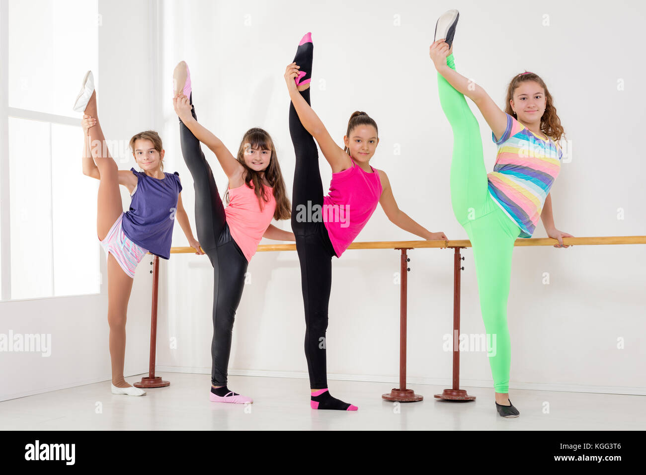 Four smiling young girls using barre while practicing in dance studio ...