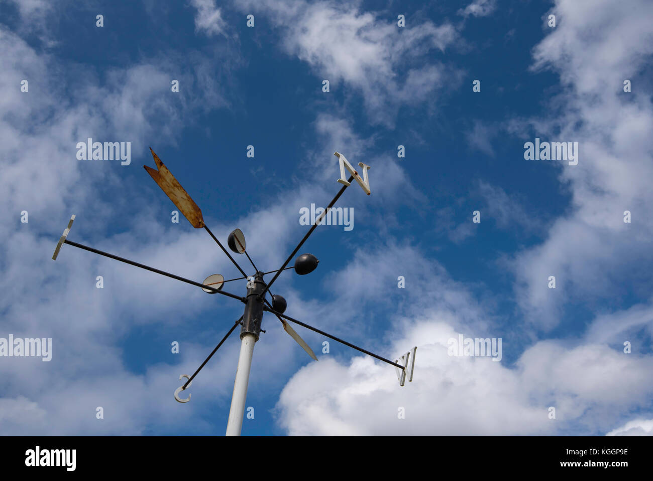 Looking up at an old weather vane or wind vane with a cloudy blue sky ...