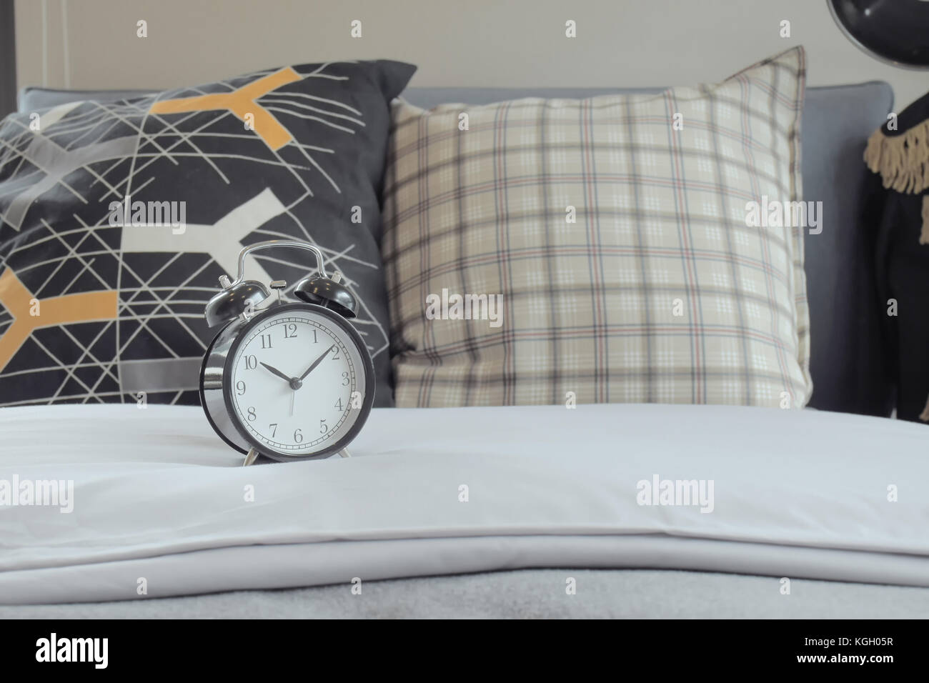 Classic style clock on white linen and grapic pattern pillows on bed ...