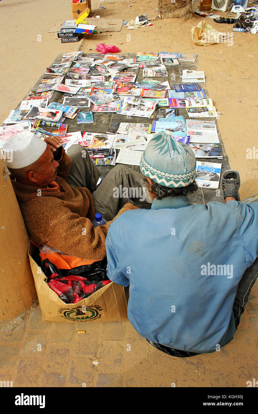 Two male vendors sitting on a floor and selling goods on the market in ...