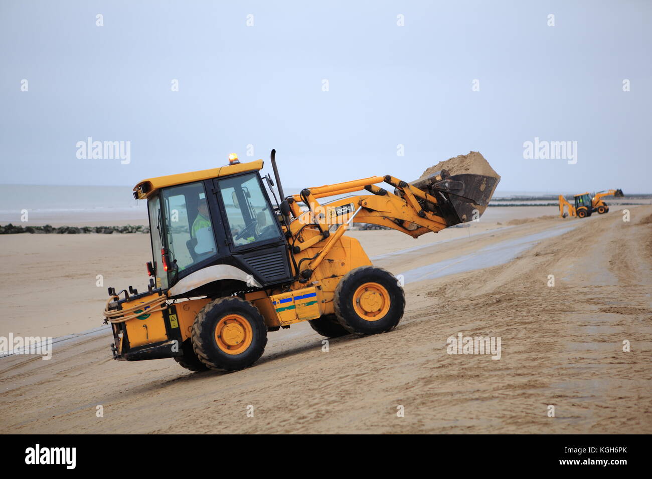 Digger moves sand on the beach at Prestatyn, North Wales for coastal ...