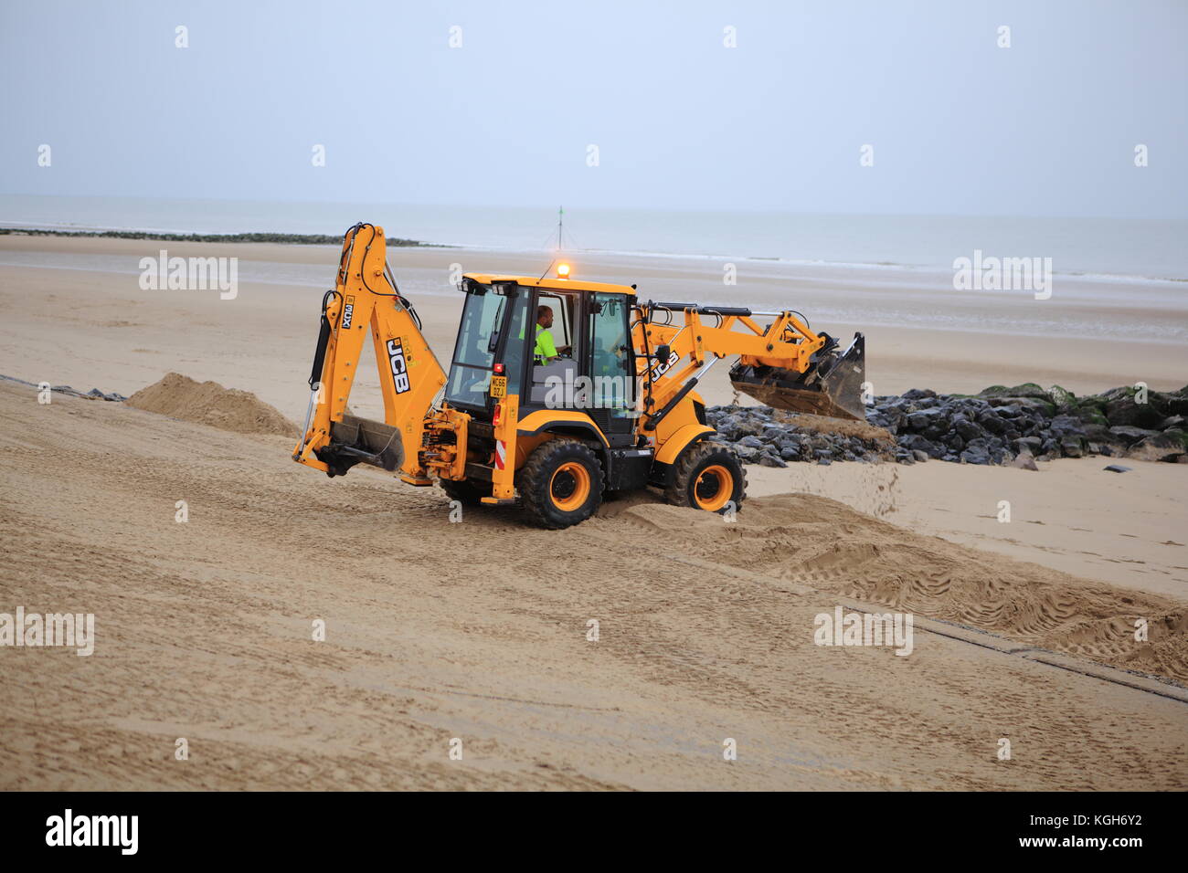 Digger moves sand on the beach at Prestatyn, North Wales for coastal ...