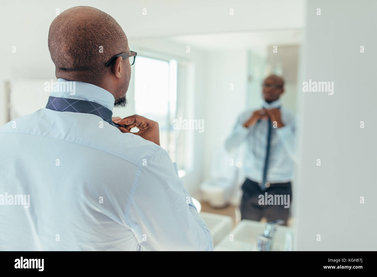 Man putting on a tie looking at a mirror. Back view of a businessman ...