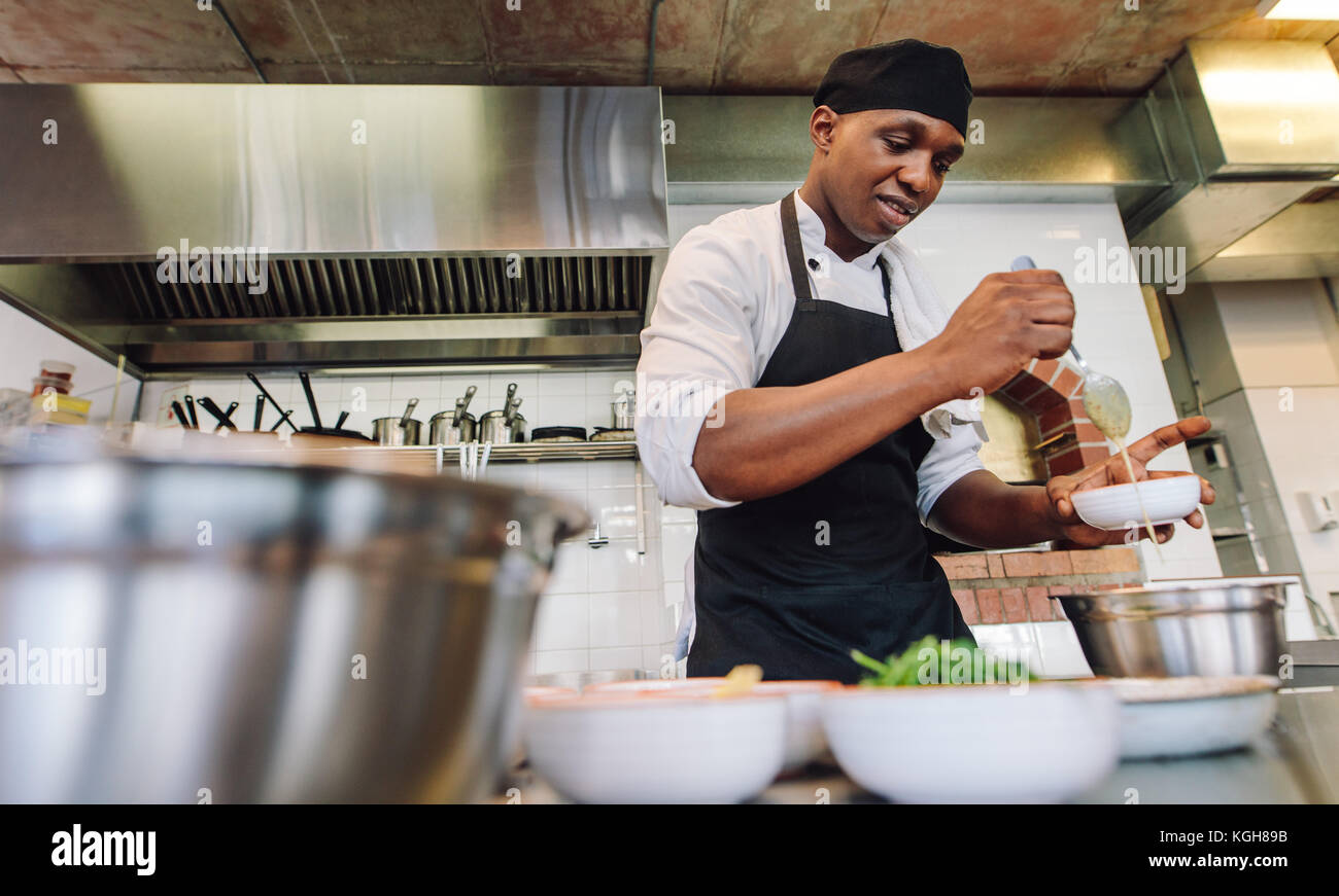 Cook adding sauce in bowl at commercial kitchen. African male chef ...