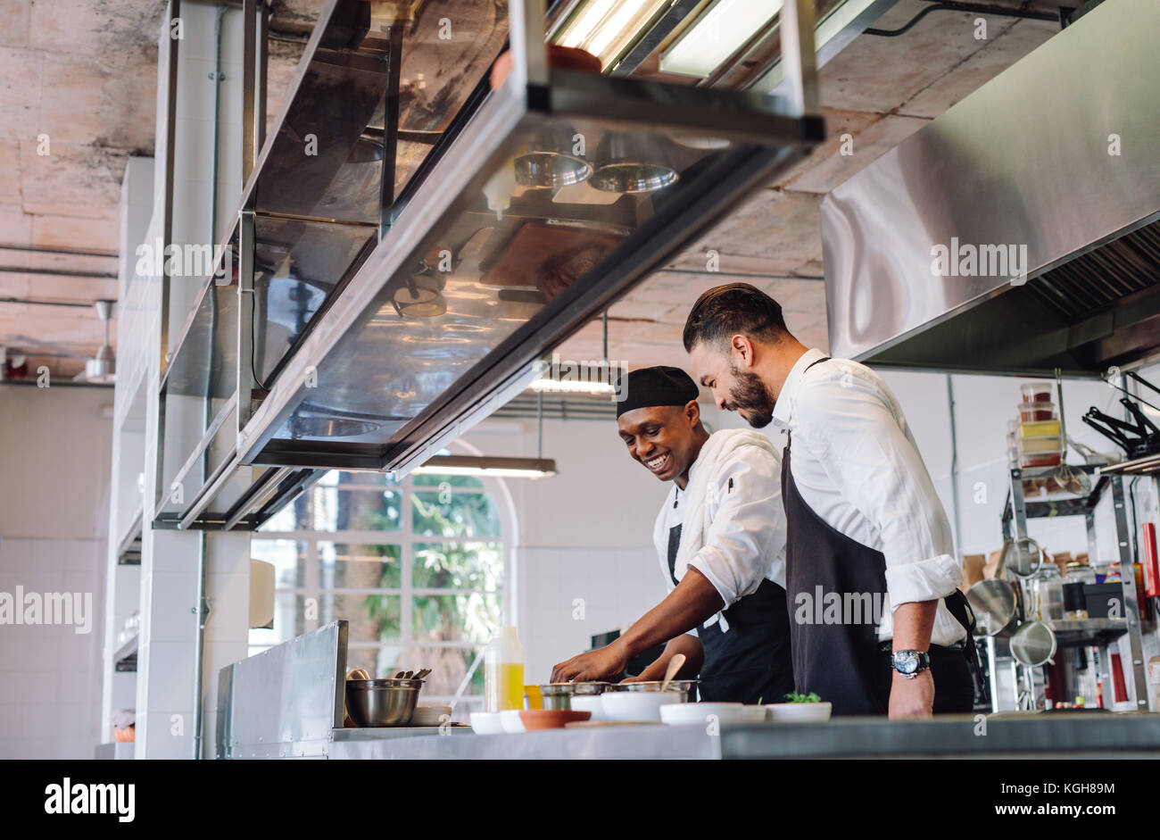 Happy male chefs cooking food at cafe kitchen and talking. Two cooks ...