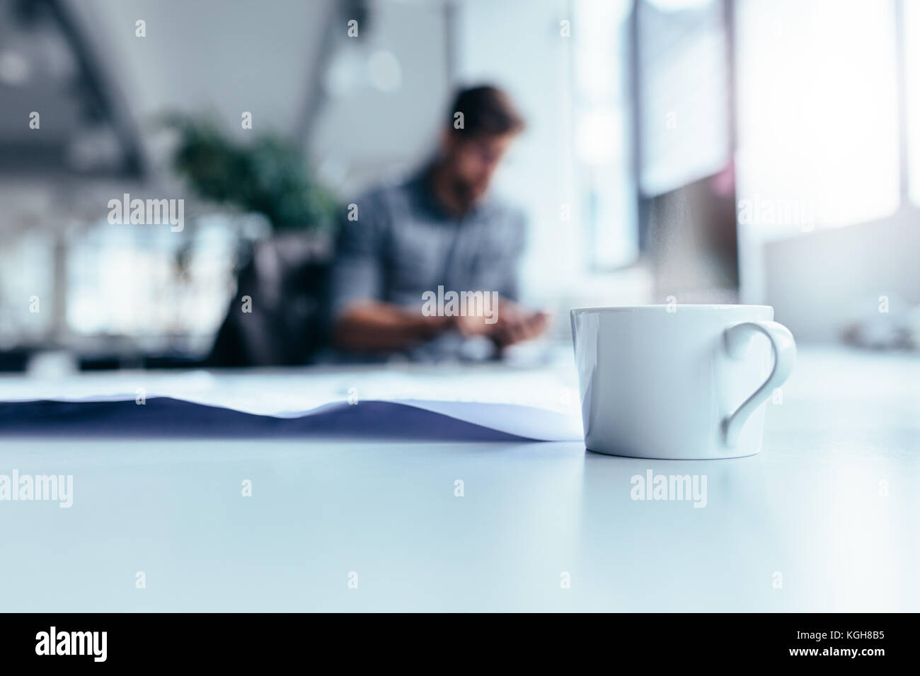 Close up of cup of coffee on desk with man working in background ...