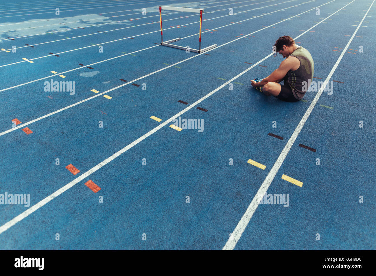 Athlete doing stretching exercises sitting on the running track. Runner ...