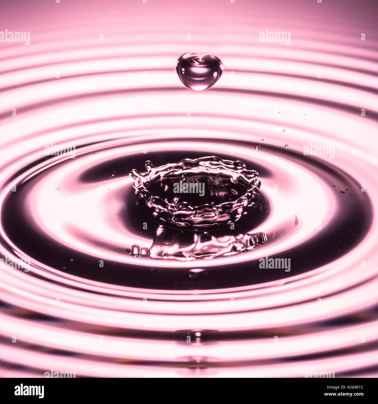 A water drop, in the shape of a heart, falls towards a splash made in a ...