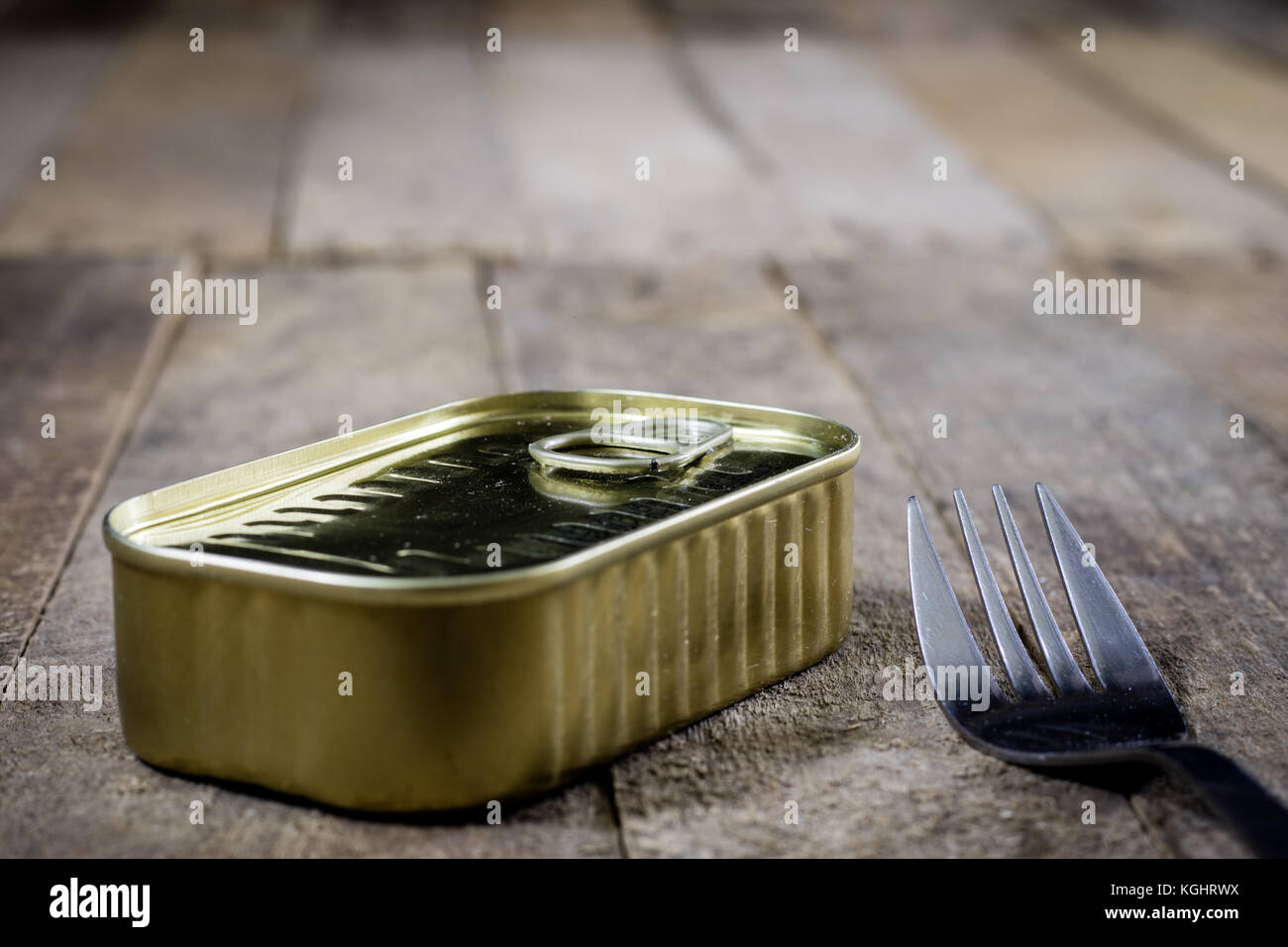 A tin can of fish on a wooden kitchen table. Next to the can fork ...