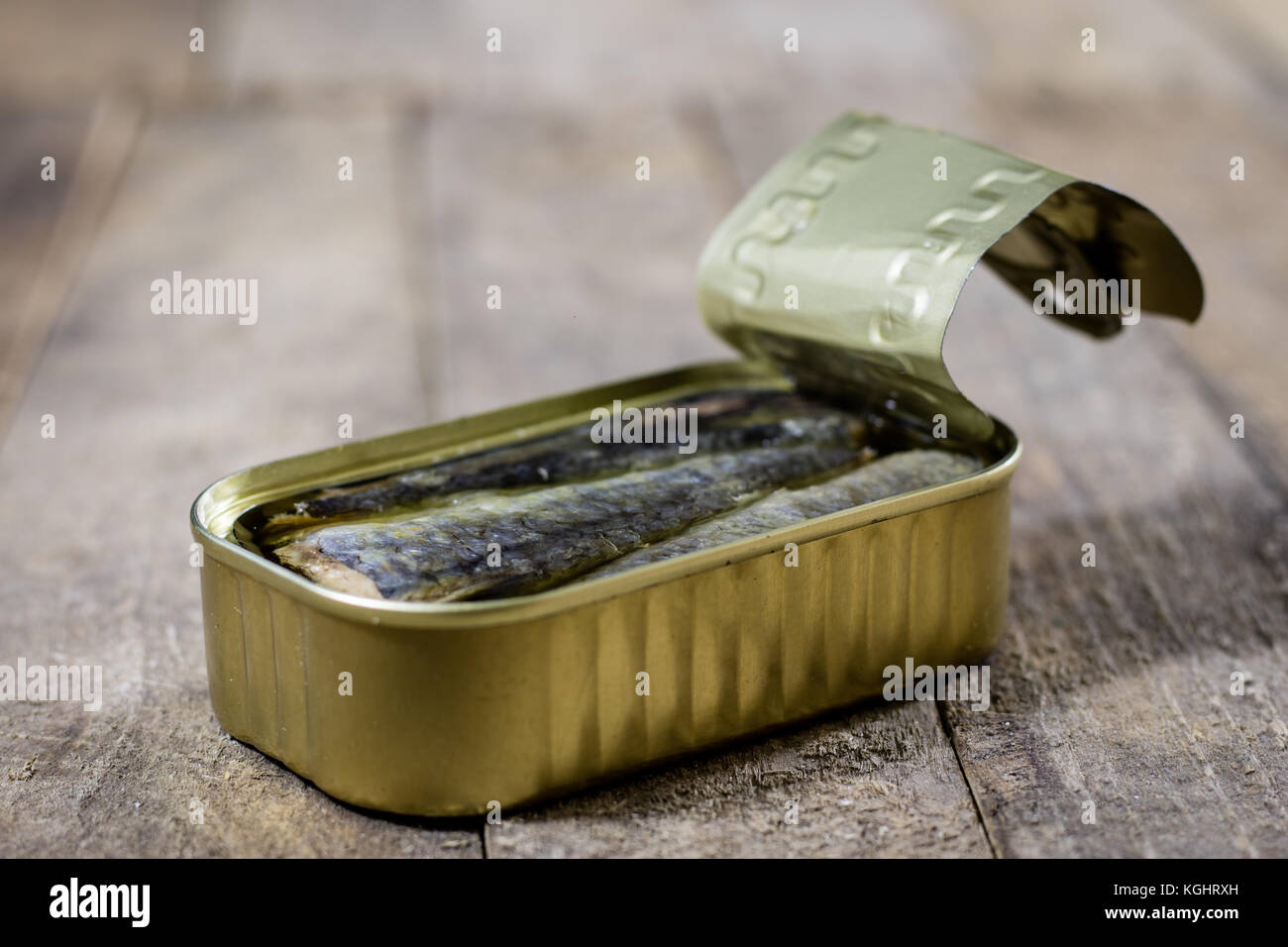 A tin can of fish on a wooden kitchen table. Next to the can fork ...